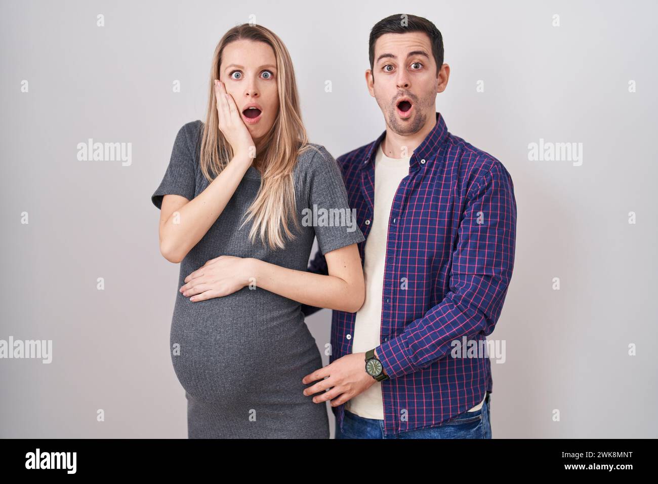 Young couple expecting a baby standing over white background afraid and ...