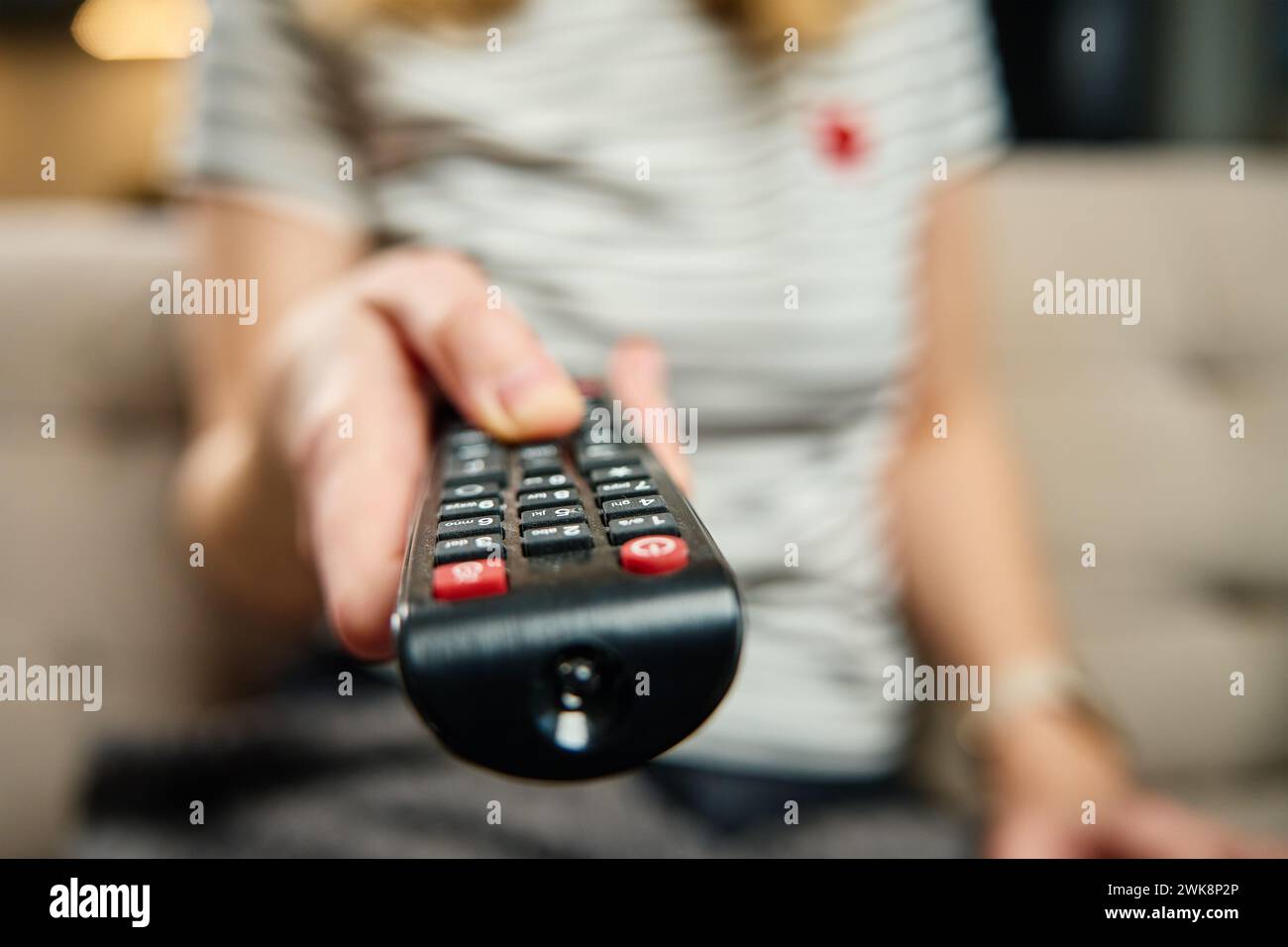 Woman holds TV remote control. Female is sitting on sofa in living room ...