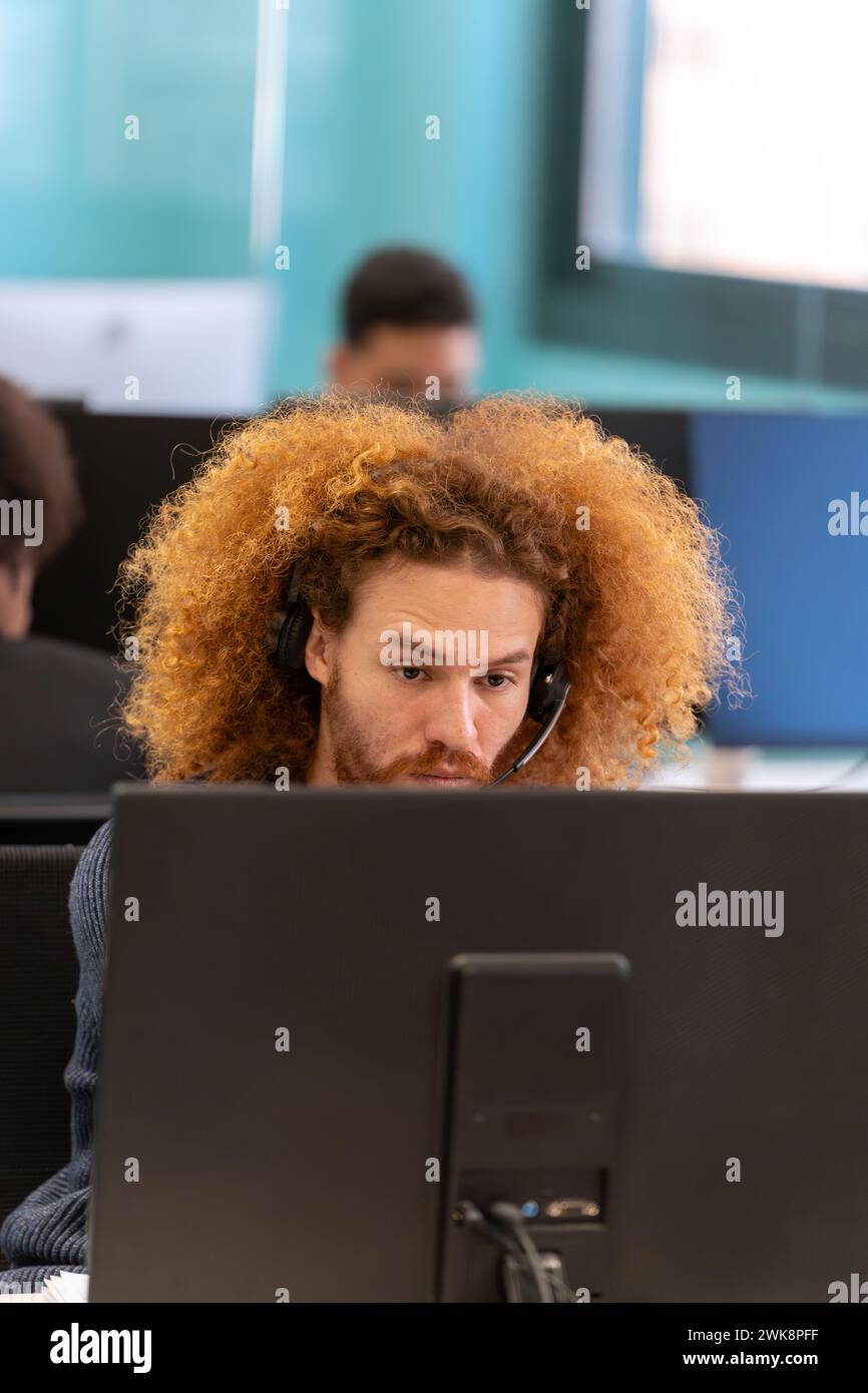Curly-haired man with headset concentrating on a computer screen in a ...