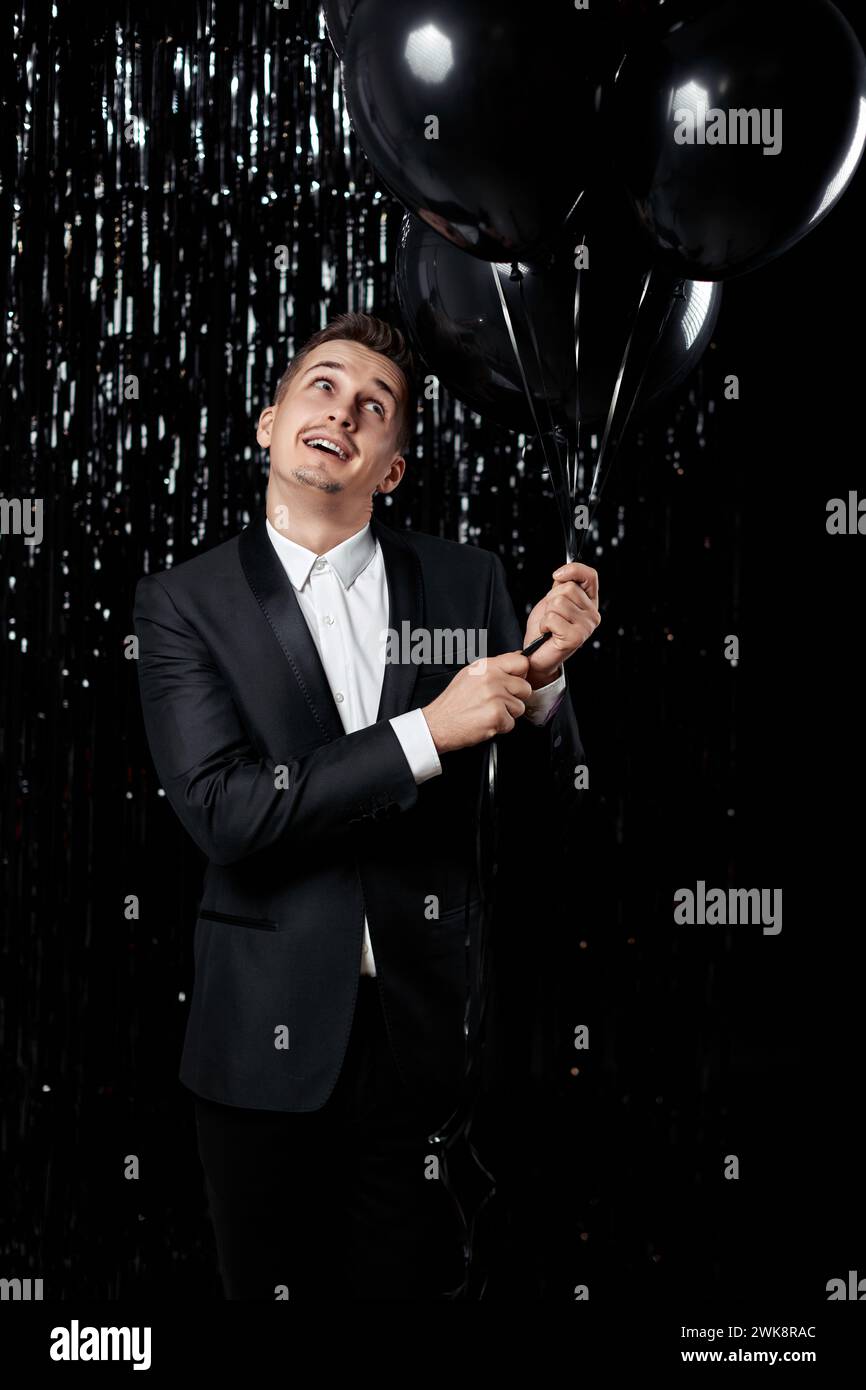 Happy handsome man in black jacket holding black air balloons on ...