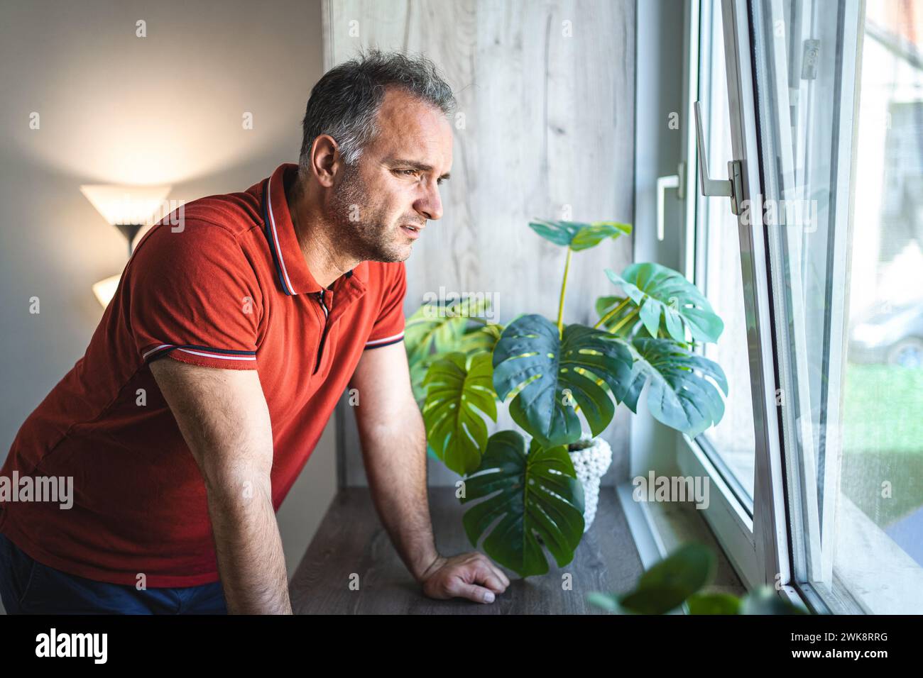 Man standing by the window looking sad and distraught Stock Photo - Alamy