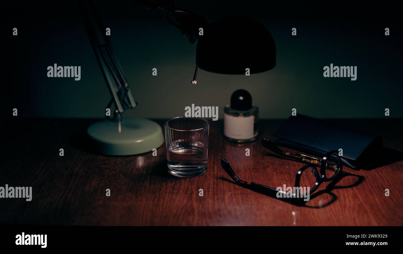 Glass of water, glasses and perfume on the table under the light of a ...