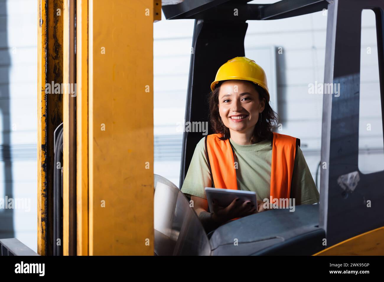 female forklift operator in hard hat and safety vest smiling and ...