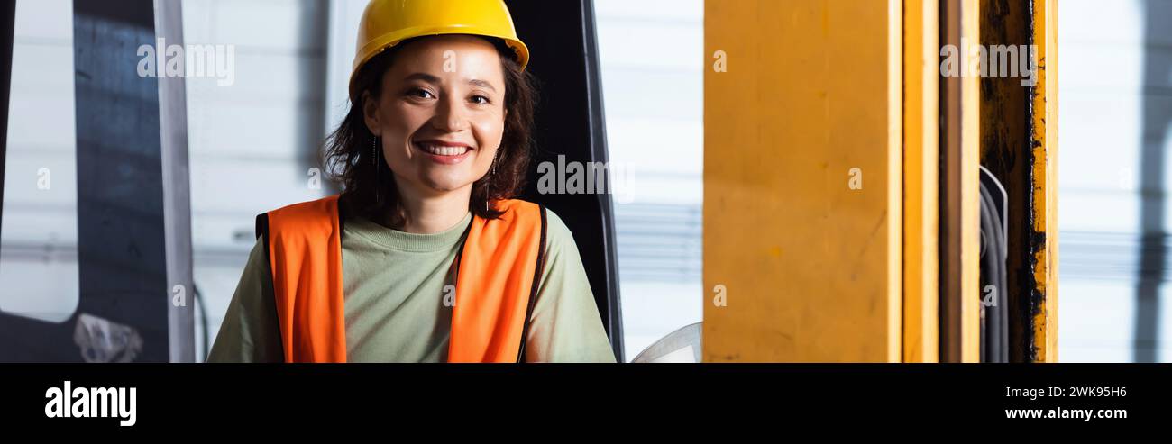 female forklift operator in hard hat and safety vest smiling in ...