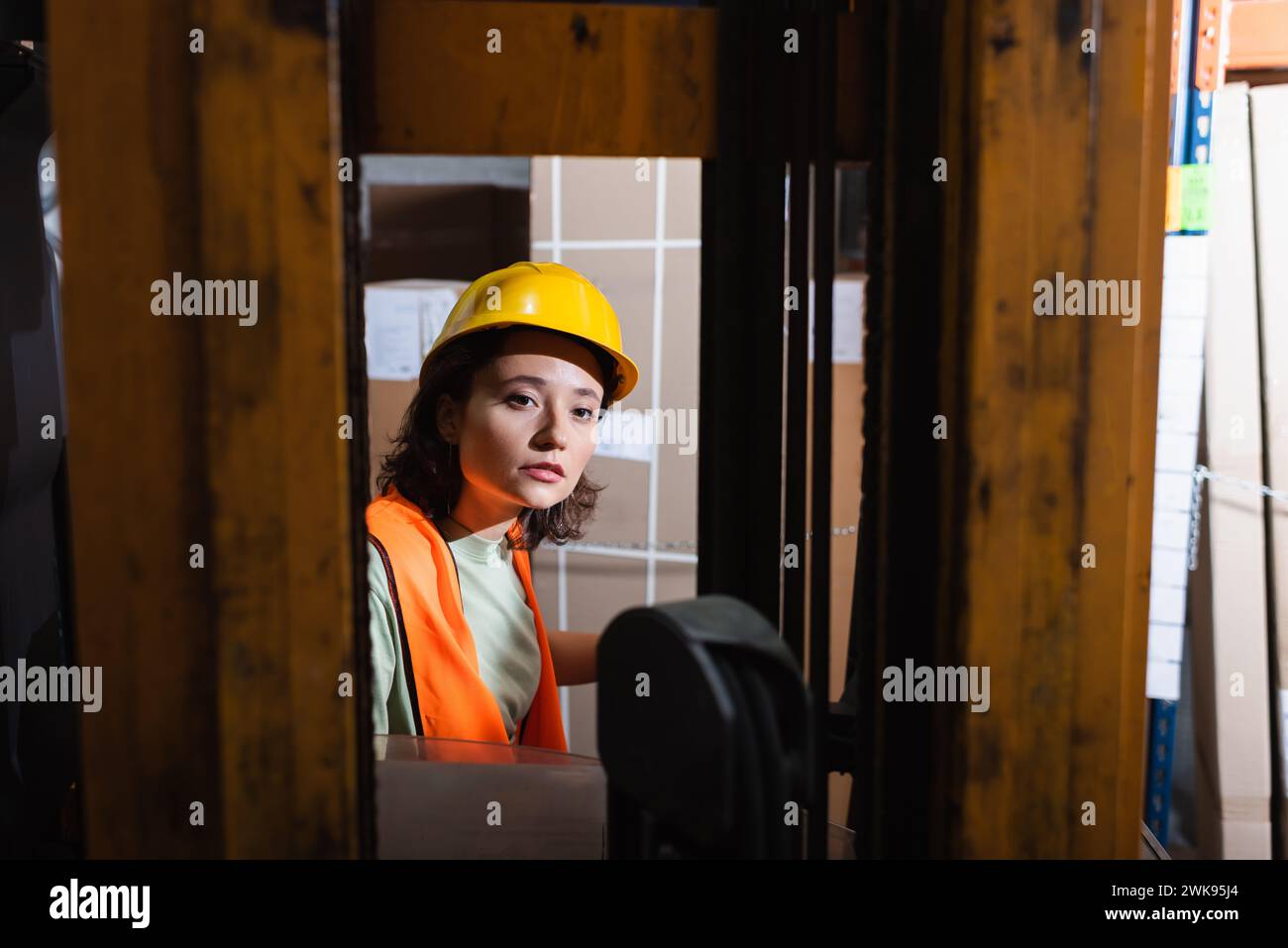 female forklift operator in hard hat and safety vest looking at camera ...