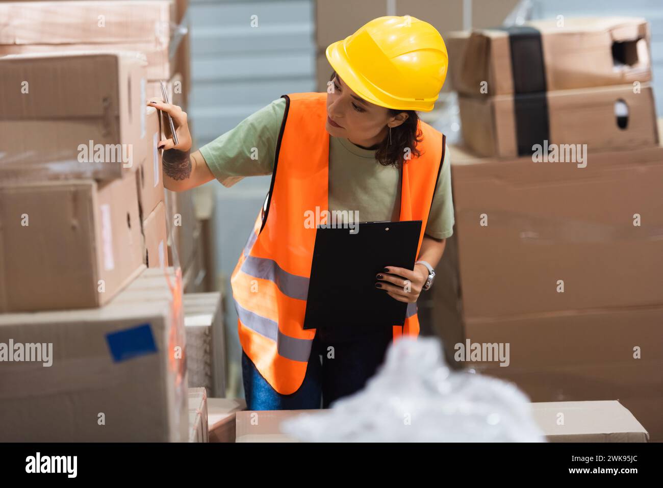 female warehouse worker in hard hat and safety vest holding clipboard ...