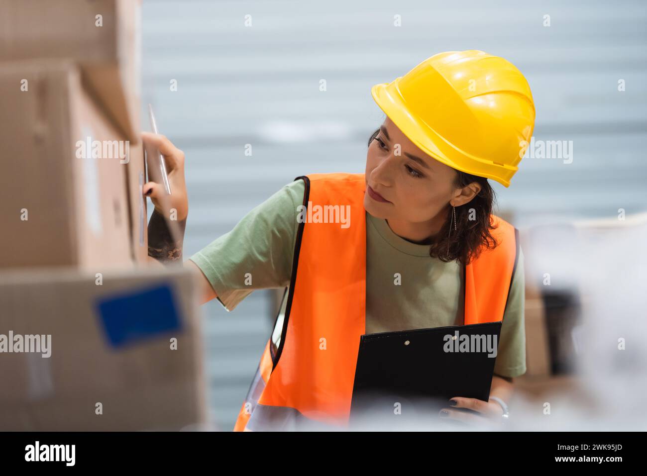 female warehouse worker in safety vest holding clipboard while checking ...