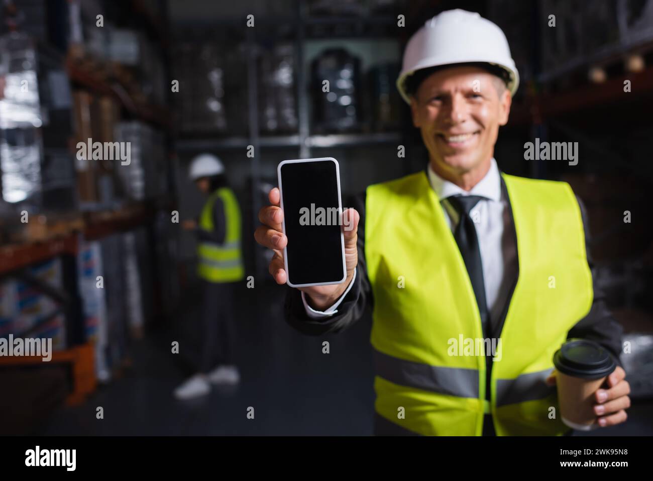happy middle aged worker in hard hat and safety vest holding coffee to ...