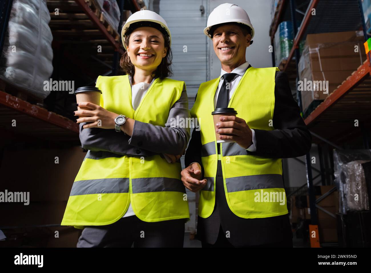 Cheerful logistics team with hard hats and coffee smiling during a ...