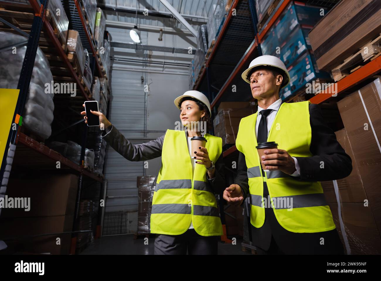 logistics team, woman in hard hat and coffee showing something to ...