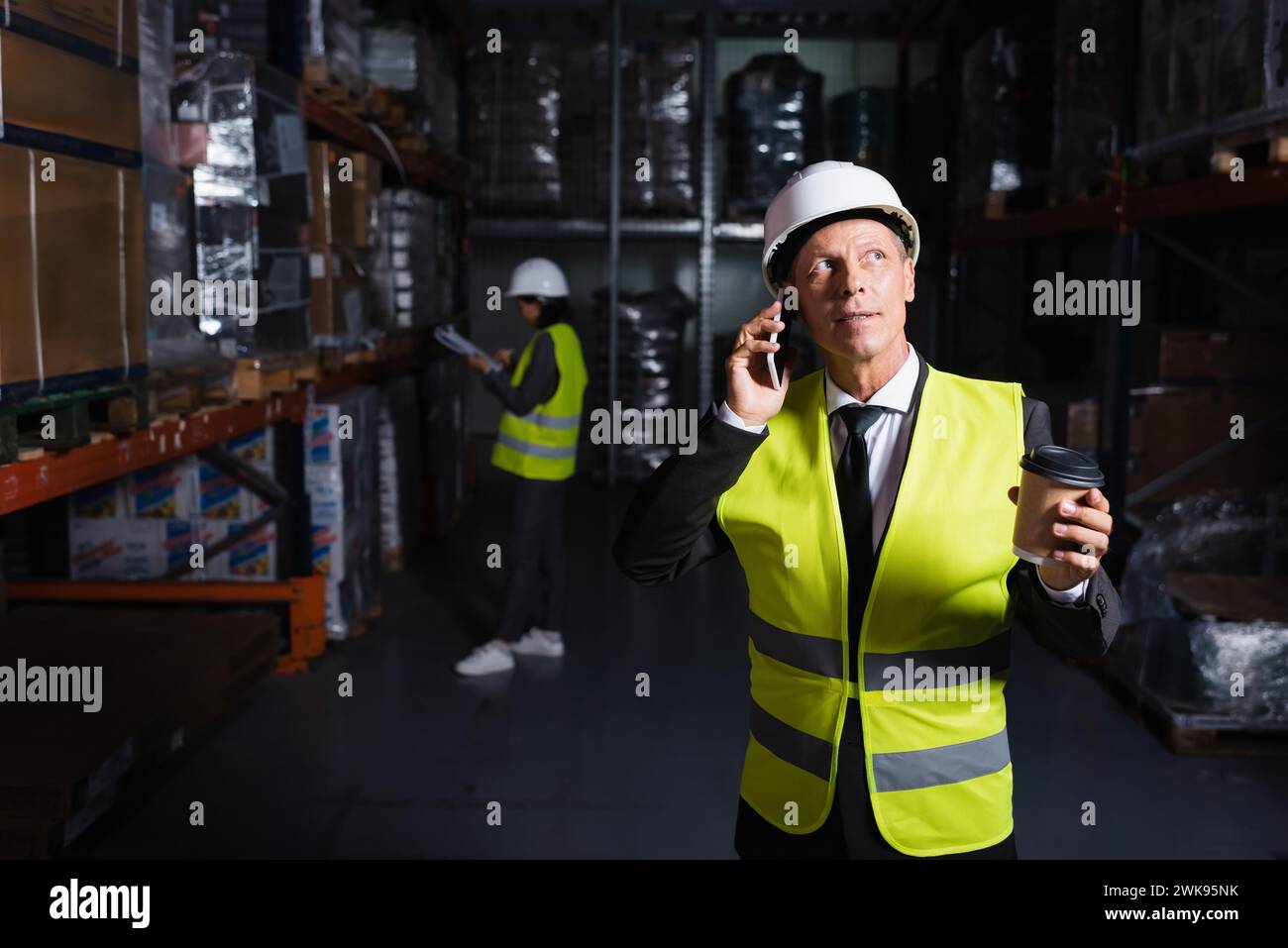 middle aged worker in hard hat and safety vest holding coffee to go ...