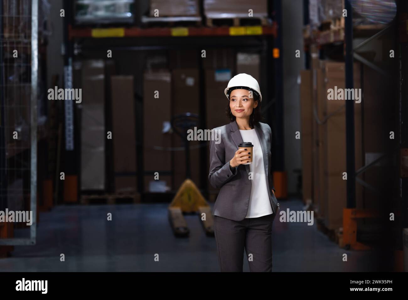 happy logistics team in hard hats walking with coffee near inventory ...