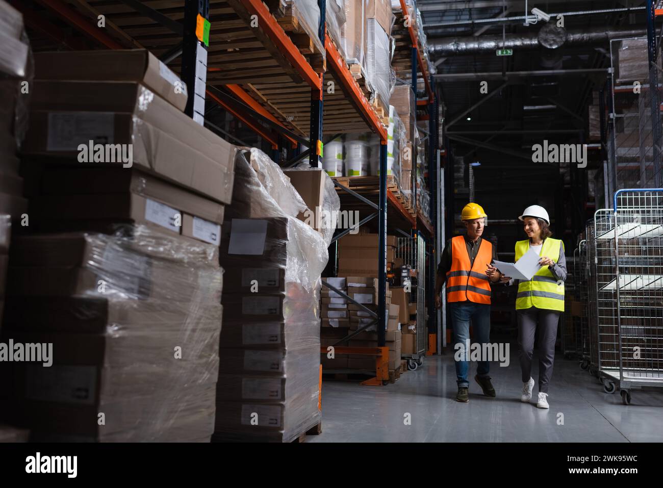 happy colleagues with hard hats walking in a well-lit warehouse and ...