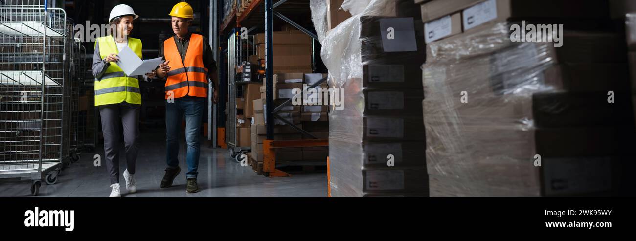 colleagues with hard hats walking in a well-lit warehouse and planning ...