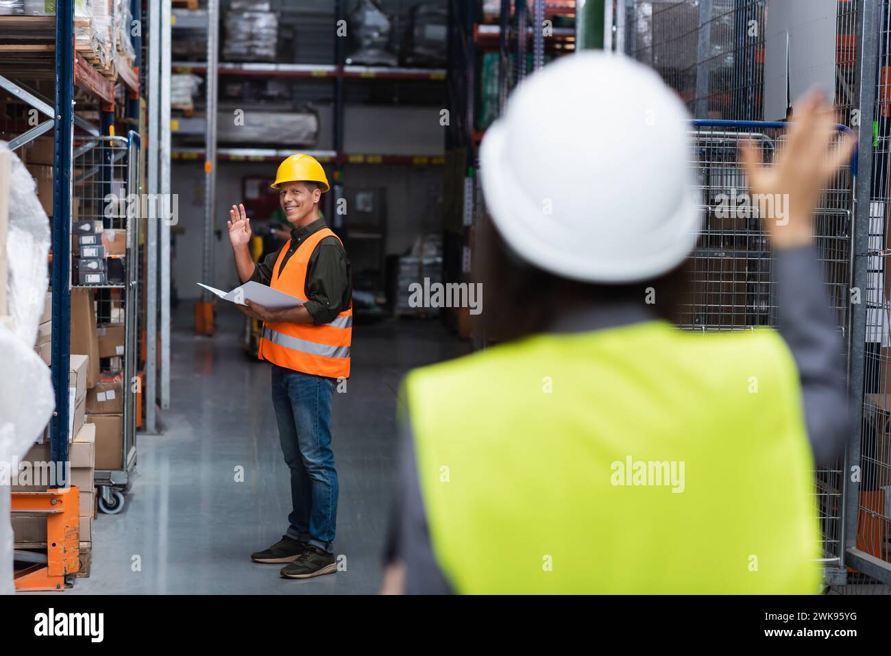 happy supervisor in hard hat waving at colleague while greeting each ...