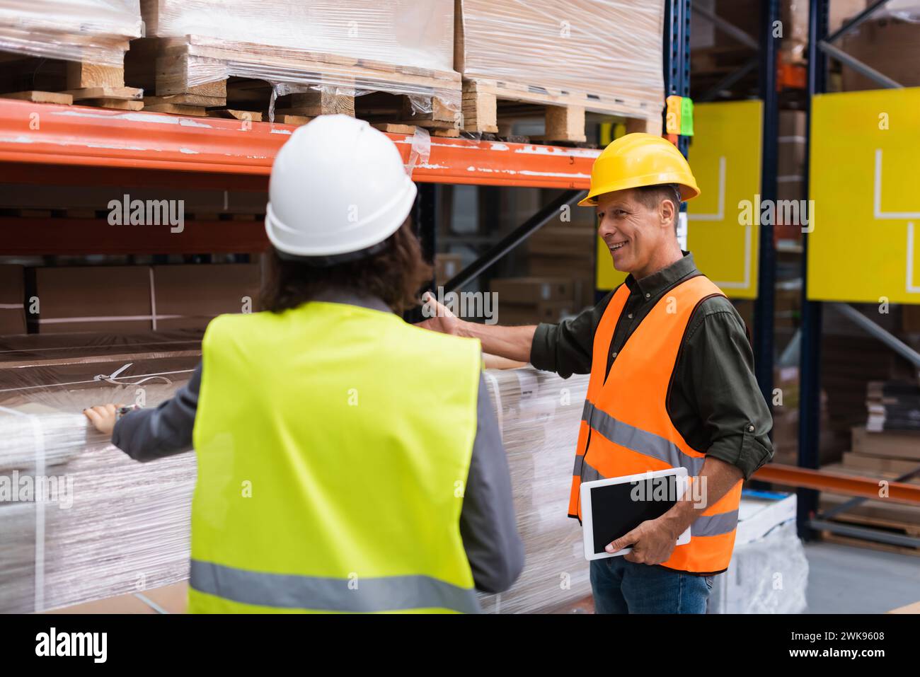 middle aged supervisor in hard hat holding tablet while explaining work ...