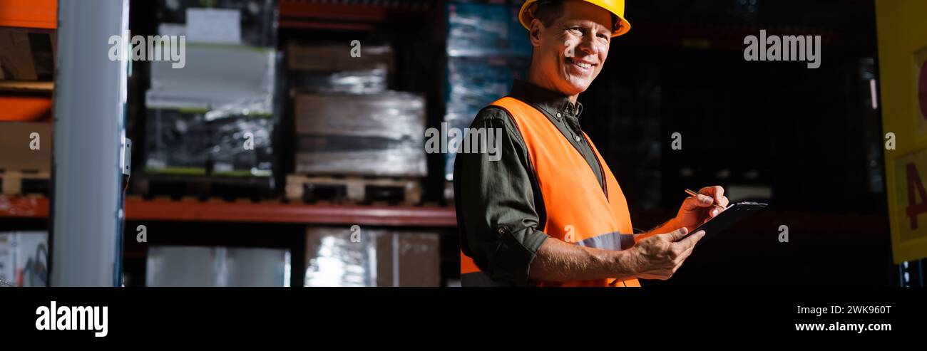 happy middle aged warehouse supervisor in hard hat with clipboard ...