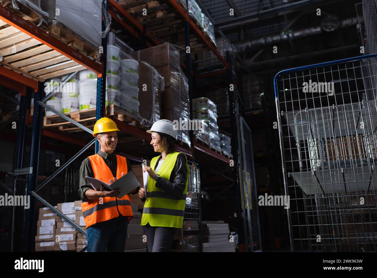 happy professionals in hard hats talking in a warehouse, middle aged ...