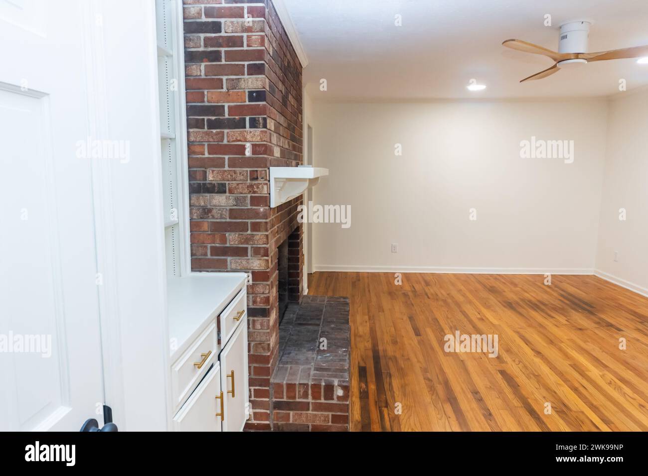 A living room or den with hardwood floors, white walls and a red brick ...