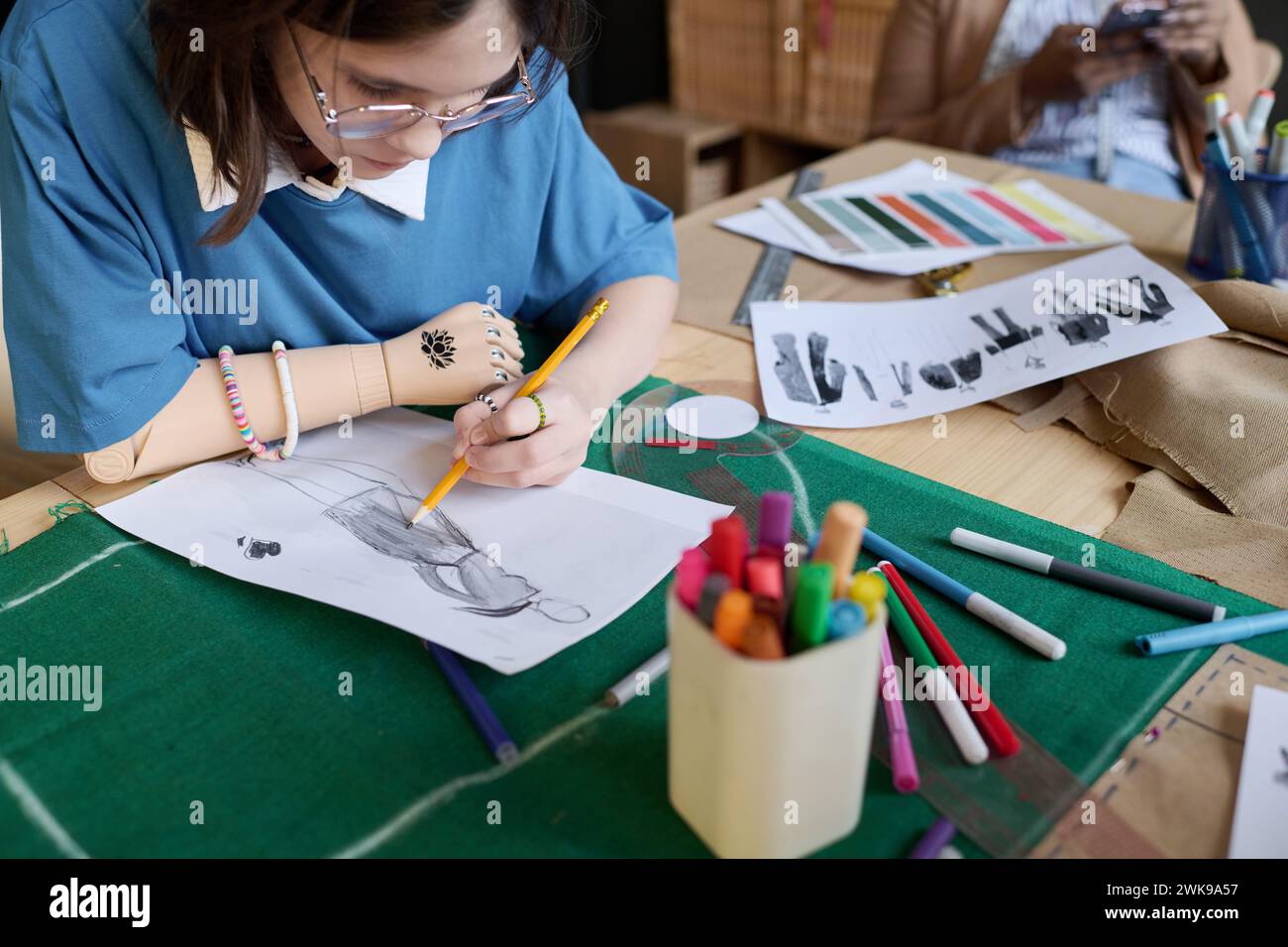 Close up of teenage girl with prosthetic hand drawing clothing sketches ...