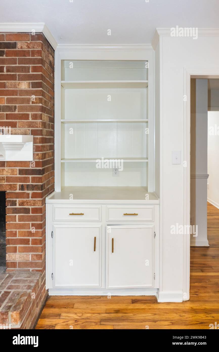 An empty white built in bookcase in a living room next to a red brick ...