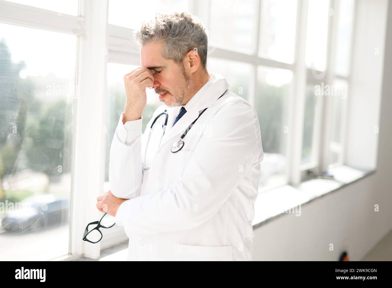 A senior doctor appears in deep contemplation, touching his temple ...