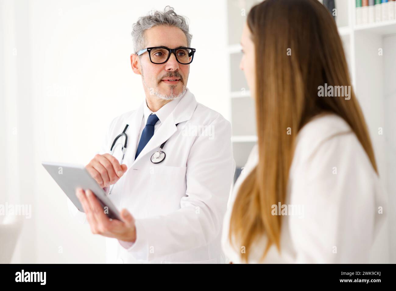 A senior doctor, with a stethoscope around his neck, attentively ...