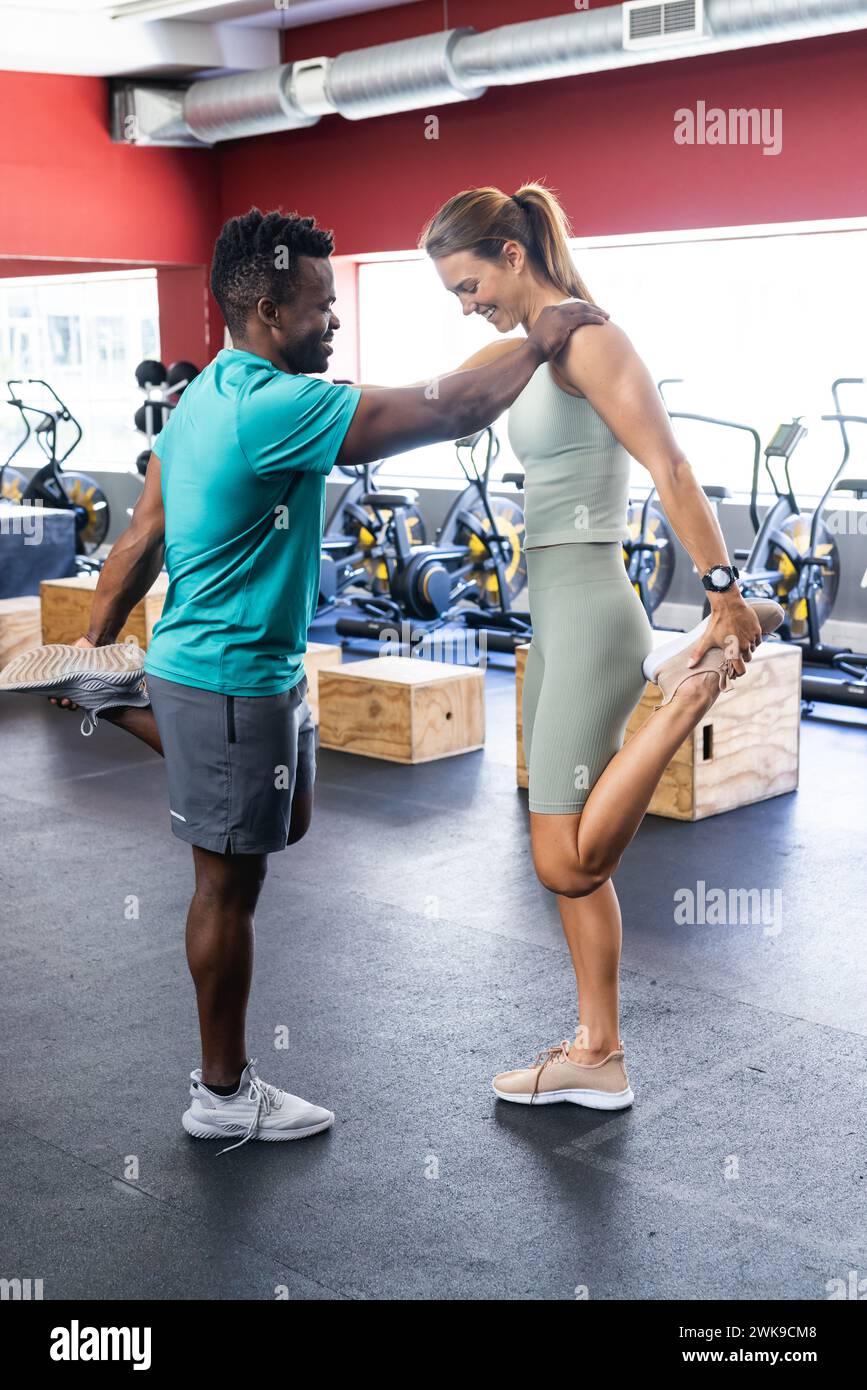 Fit African American man assists young fit Caucasian woman in a gym ...