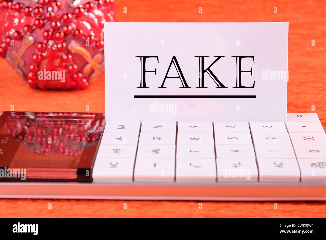 FAKE word written on a white business card on a calculator on an orange ...