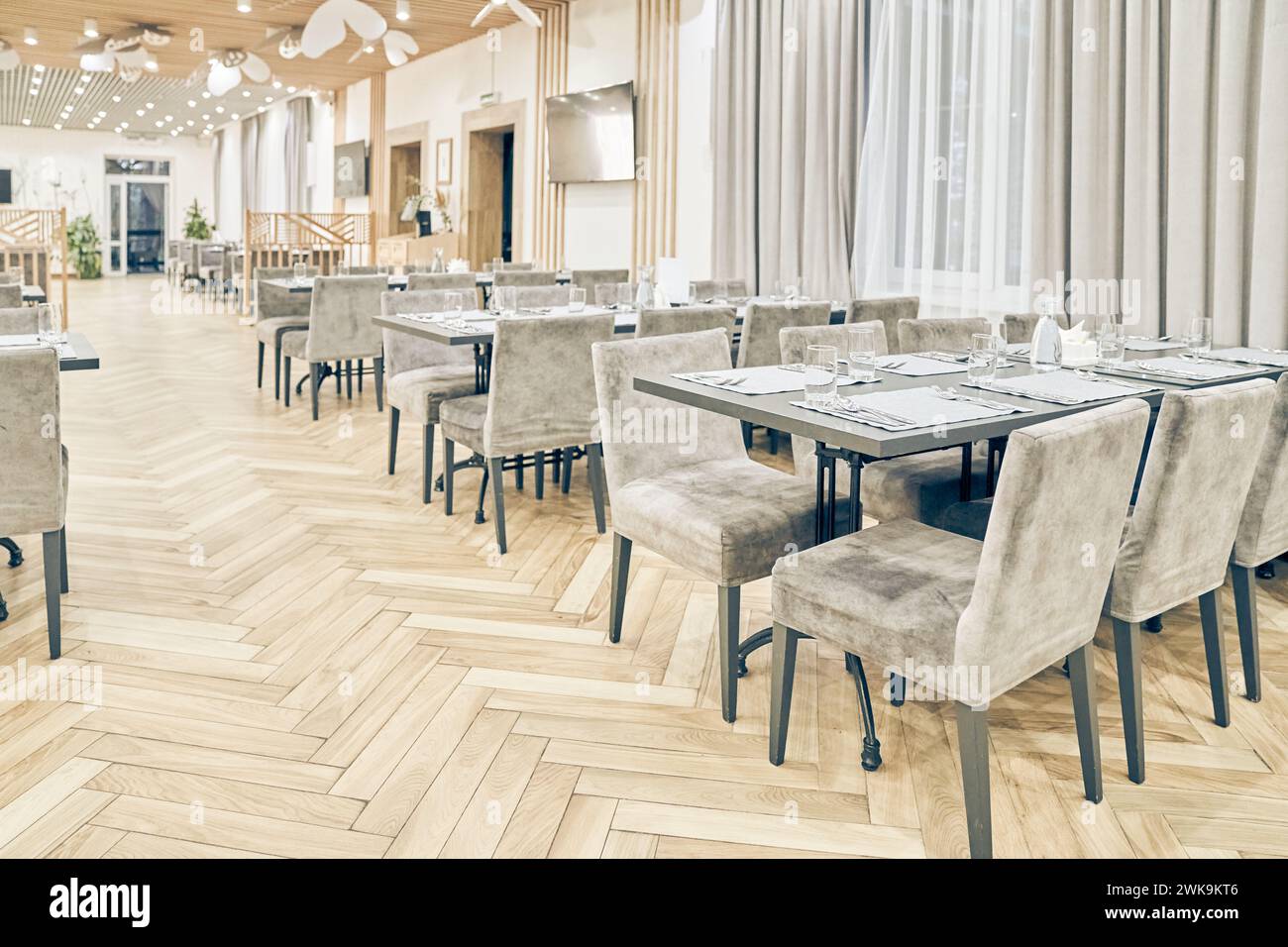 Side view of a large empty bright restaurant with tables, soft chairs ...