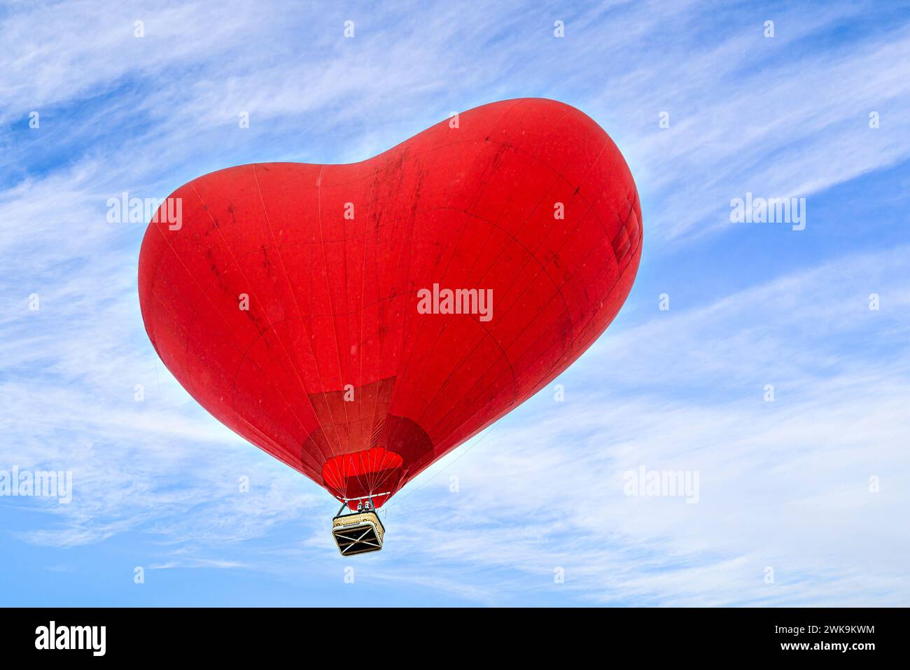 Red heart-shaped hot air balloon flying over a blue sky with white ...