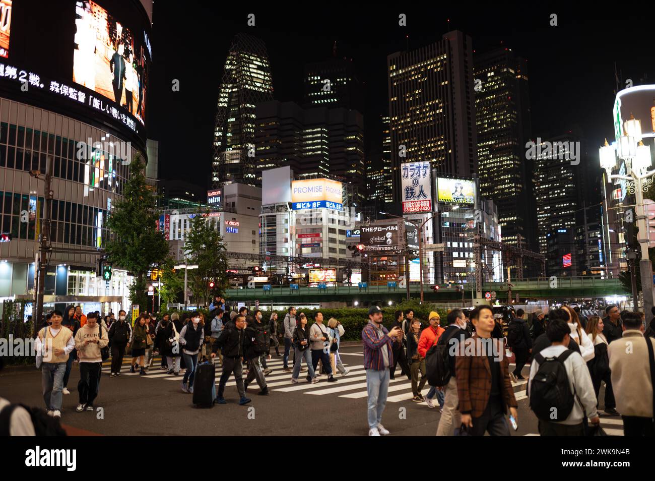 Pedestrians cross at a busy Shinjuku intersection under the night-time ...