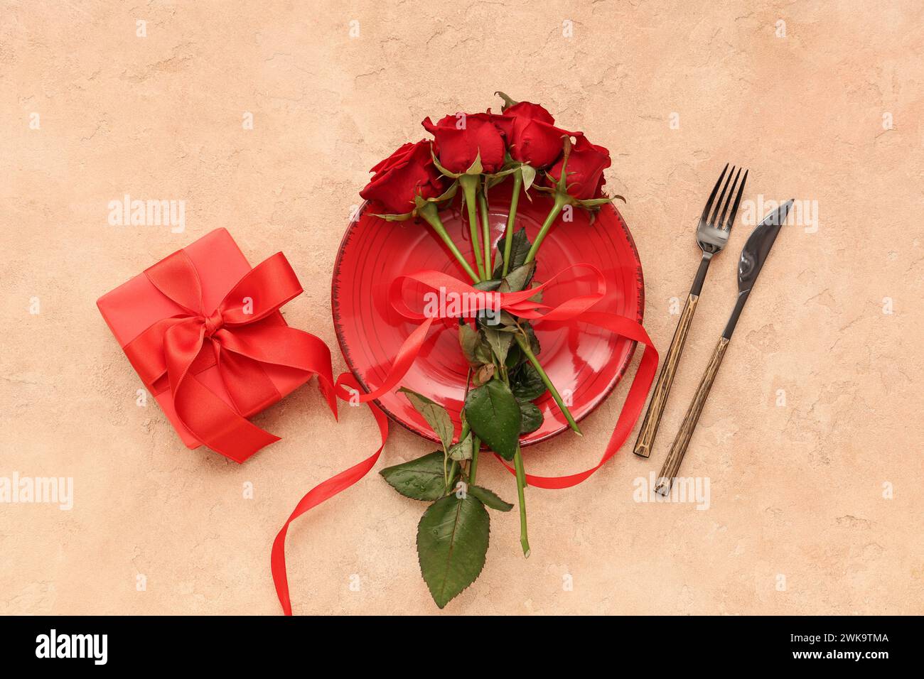 Beautiful table setting with red roses and gift box on beige background ...