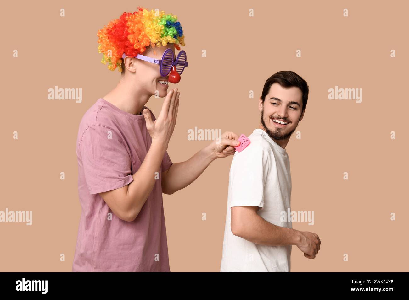 Young man sticking paper on his friend's back against brown background ...