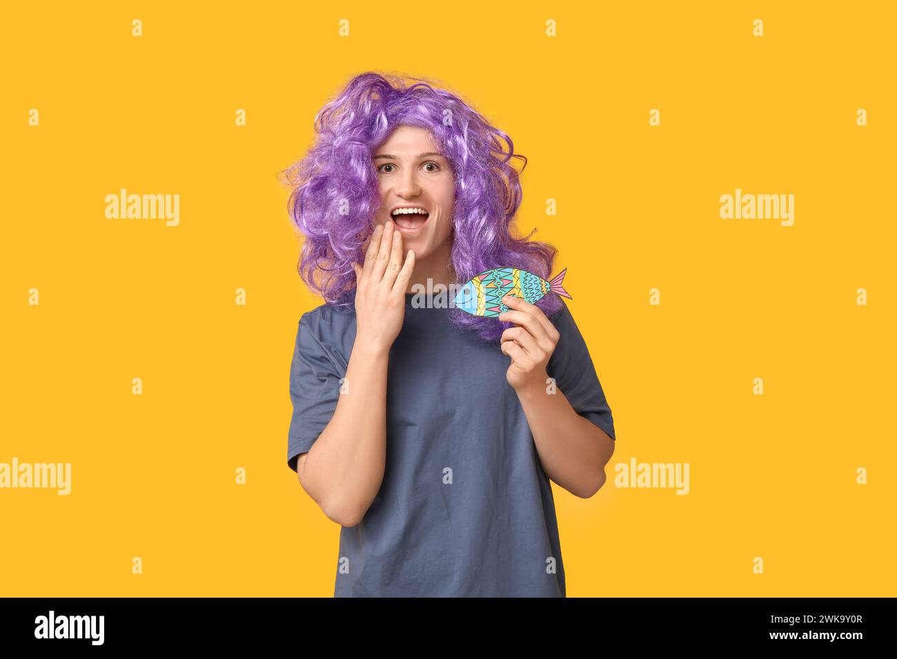 Handsome young shocked man in funny disguise with paper fish on yellow ...