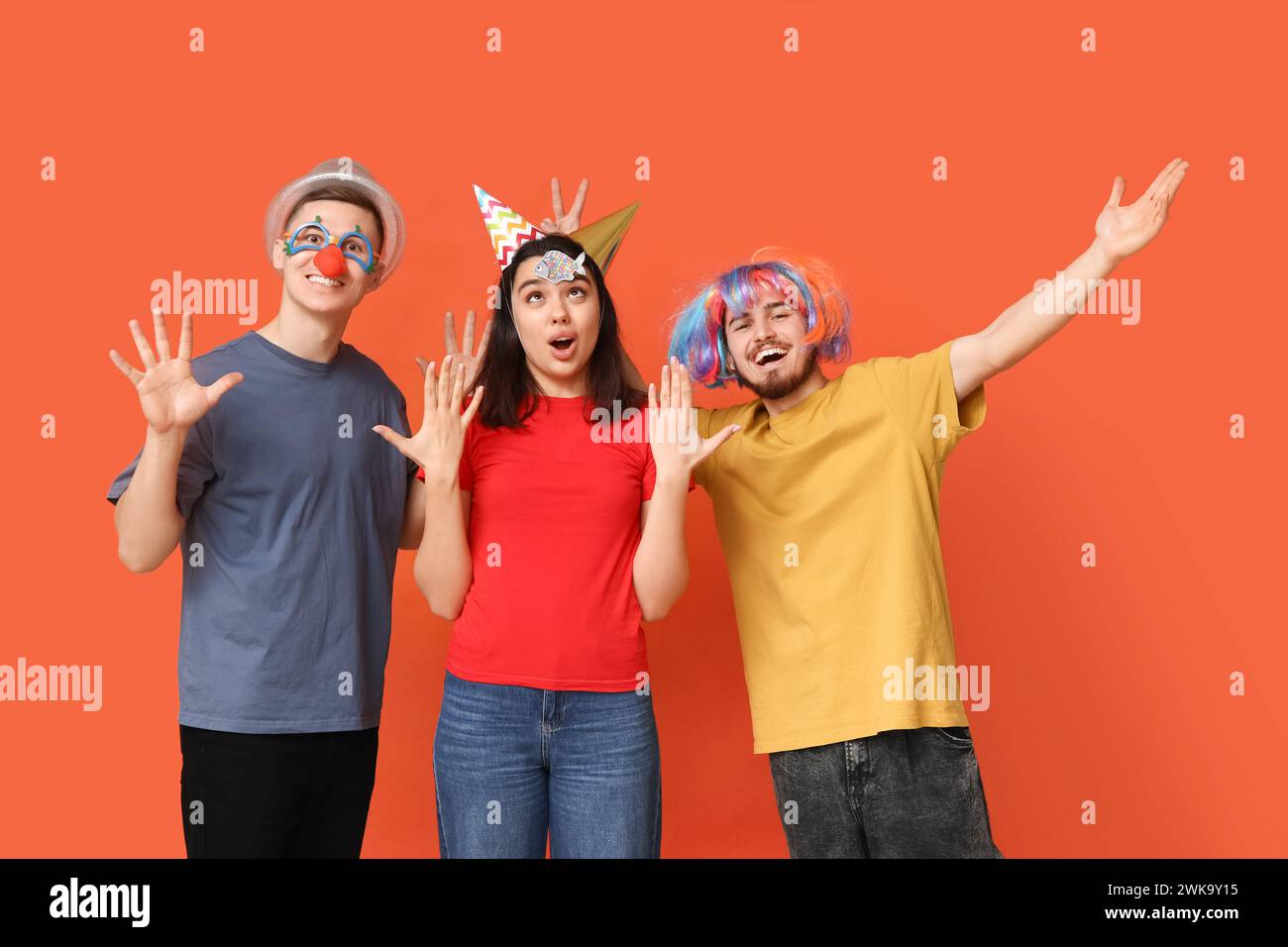 Young shocked friends in funny disguise with paper fish on orange ...