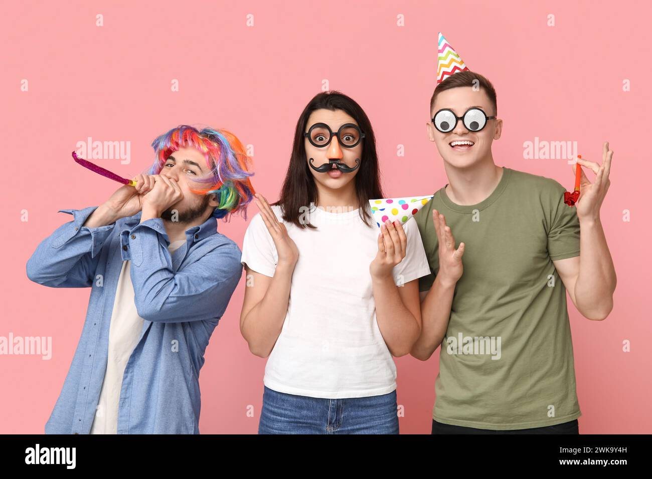 Young friends in funny disguise with party whistles on pink background ...