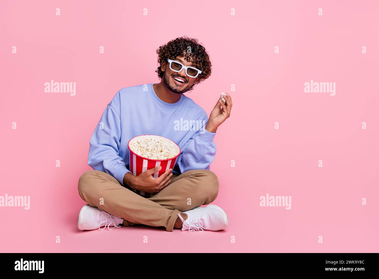 Full length photo of handsome young male sit floor eat popcorn watch ...