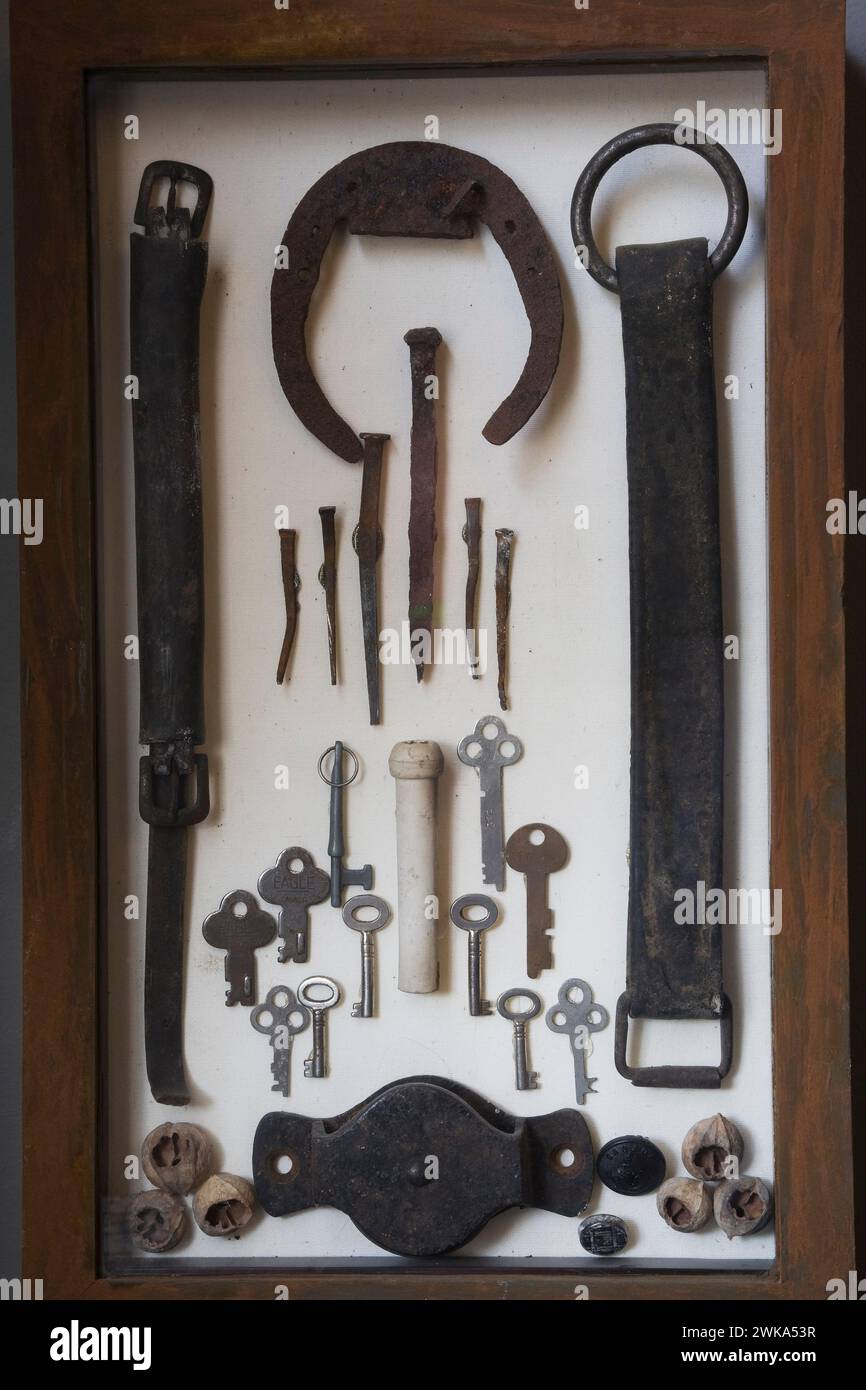 A collection of assorted keys, nails and leather straps behind a framed ...