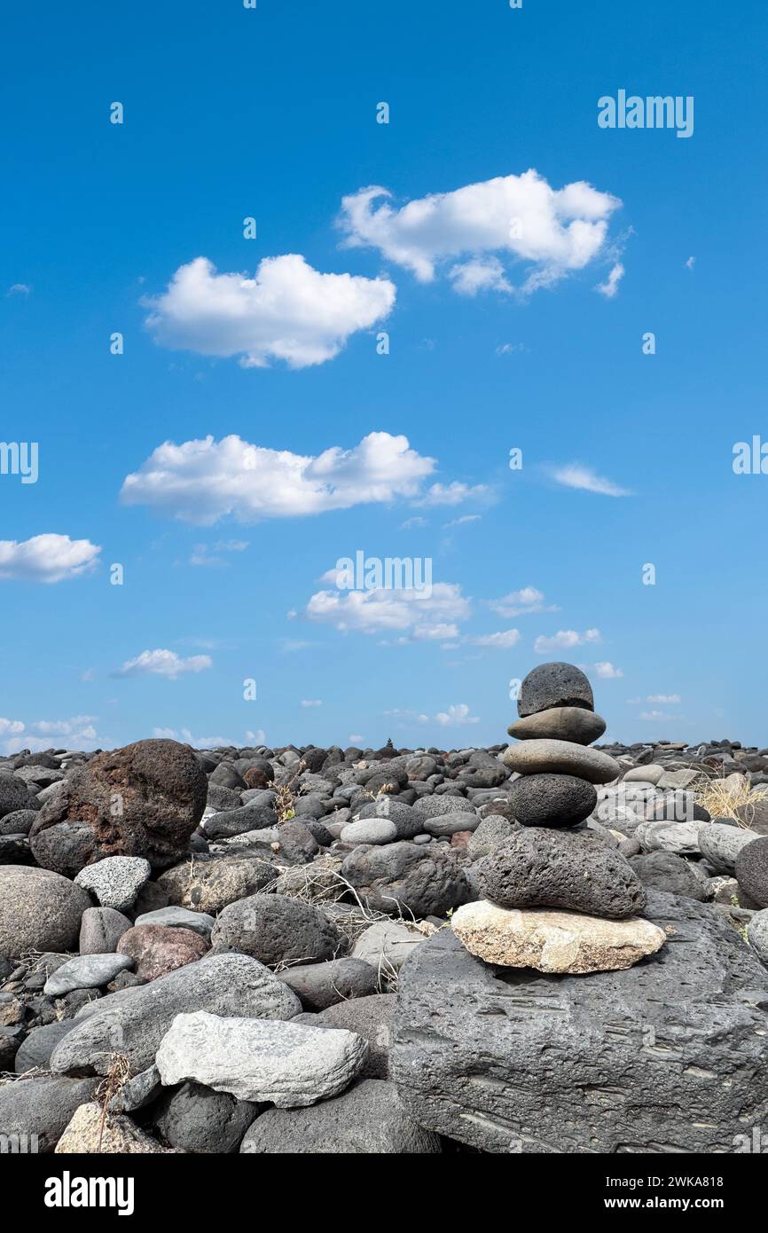 Zen-like stone pyramid on a wild volcanic shore with blue sky, clouds ...