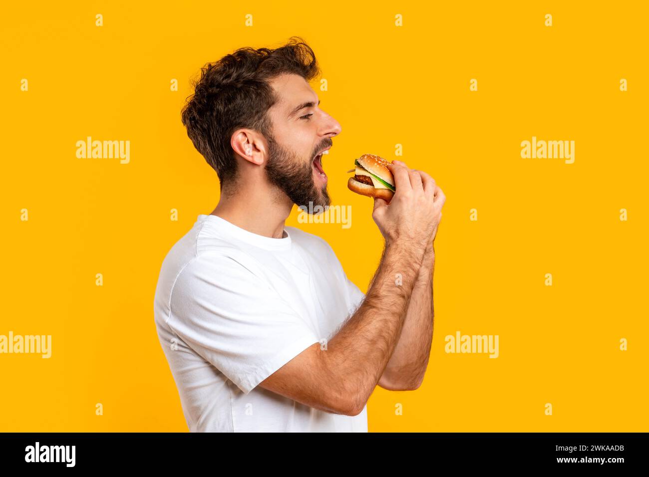 Side View Of Hungry Man Biting Big Burger In Studio Stock Photo - Alamy