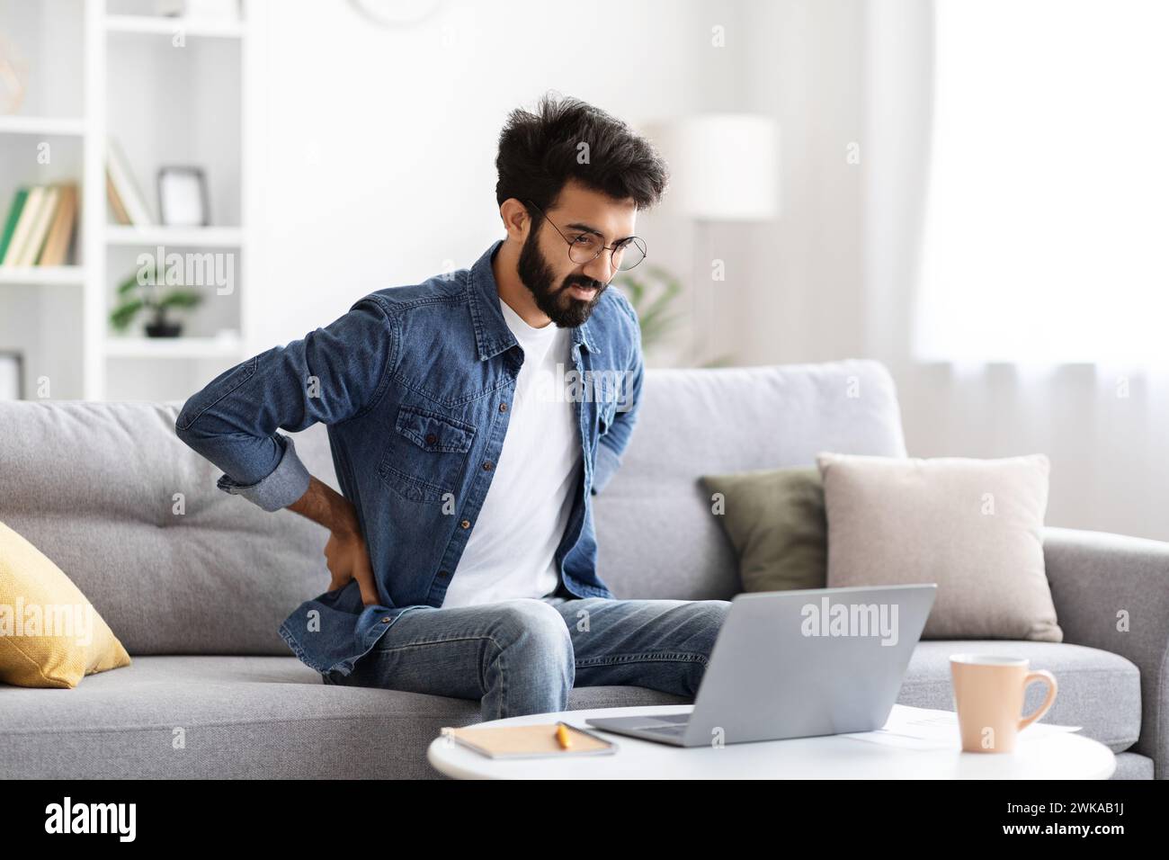 Young indian man experiencing back pain while working on laptop at home ...