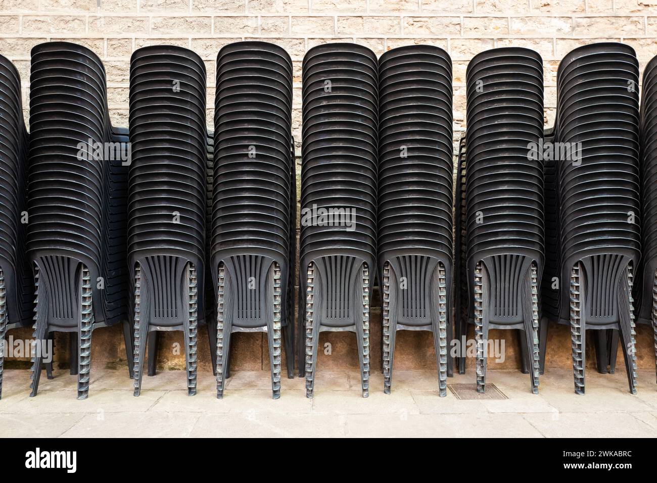 Black plastic chairs stacked on top of each other against a wall. event ...