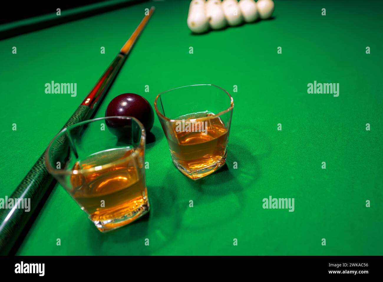 Two glass of whiskey on billiard table with cue and billiard balls in ...