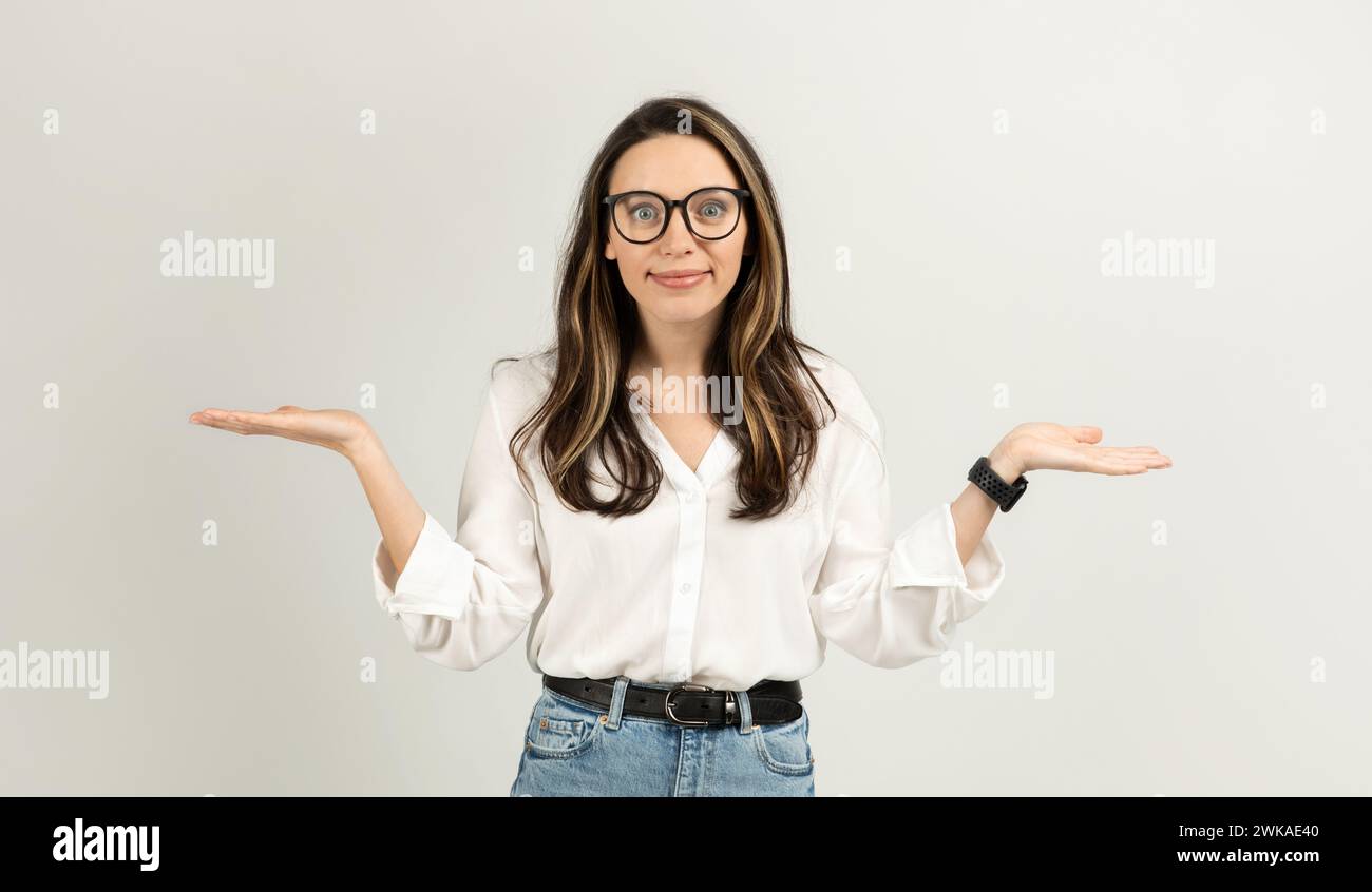A young woman with brown hair and glasses raises her hands with palms ...
