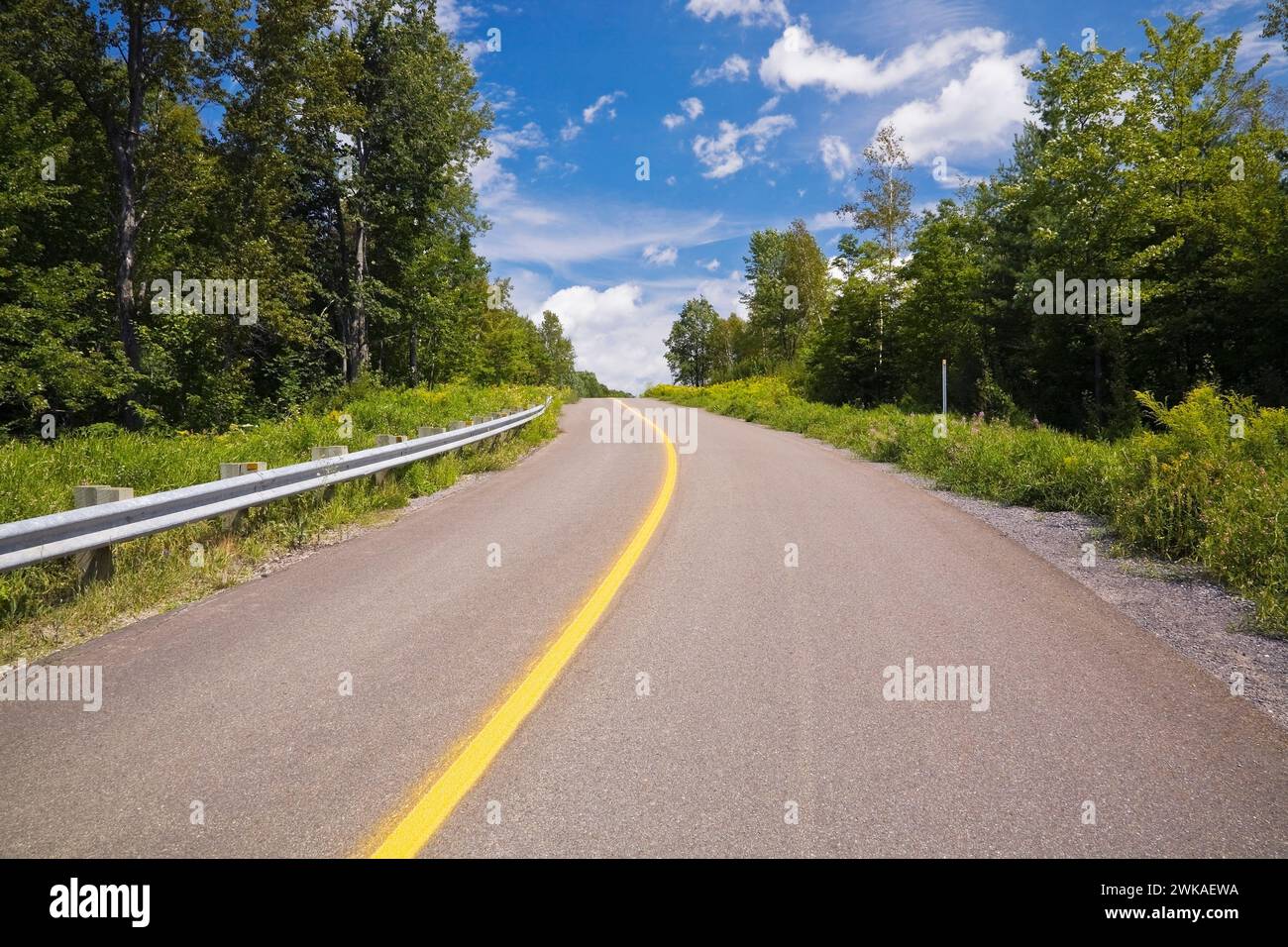Winding country road in summer with solid yellow dividing traffic line ...