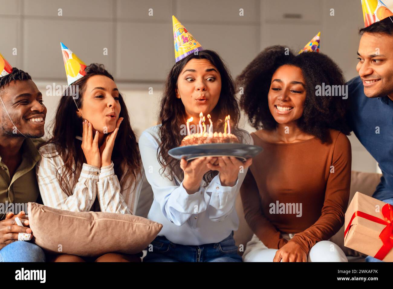 multicultural friends gathering in living room to celebrate birthday ...