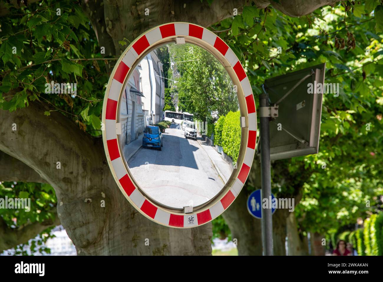 A round traffic mirror with a red and white border and a street in the ...