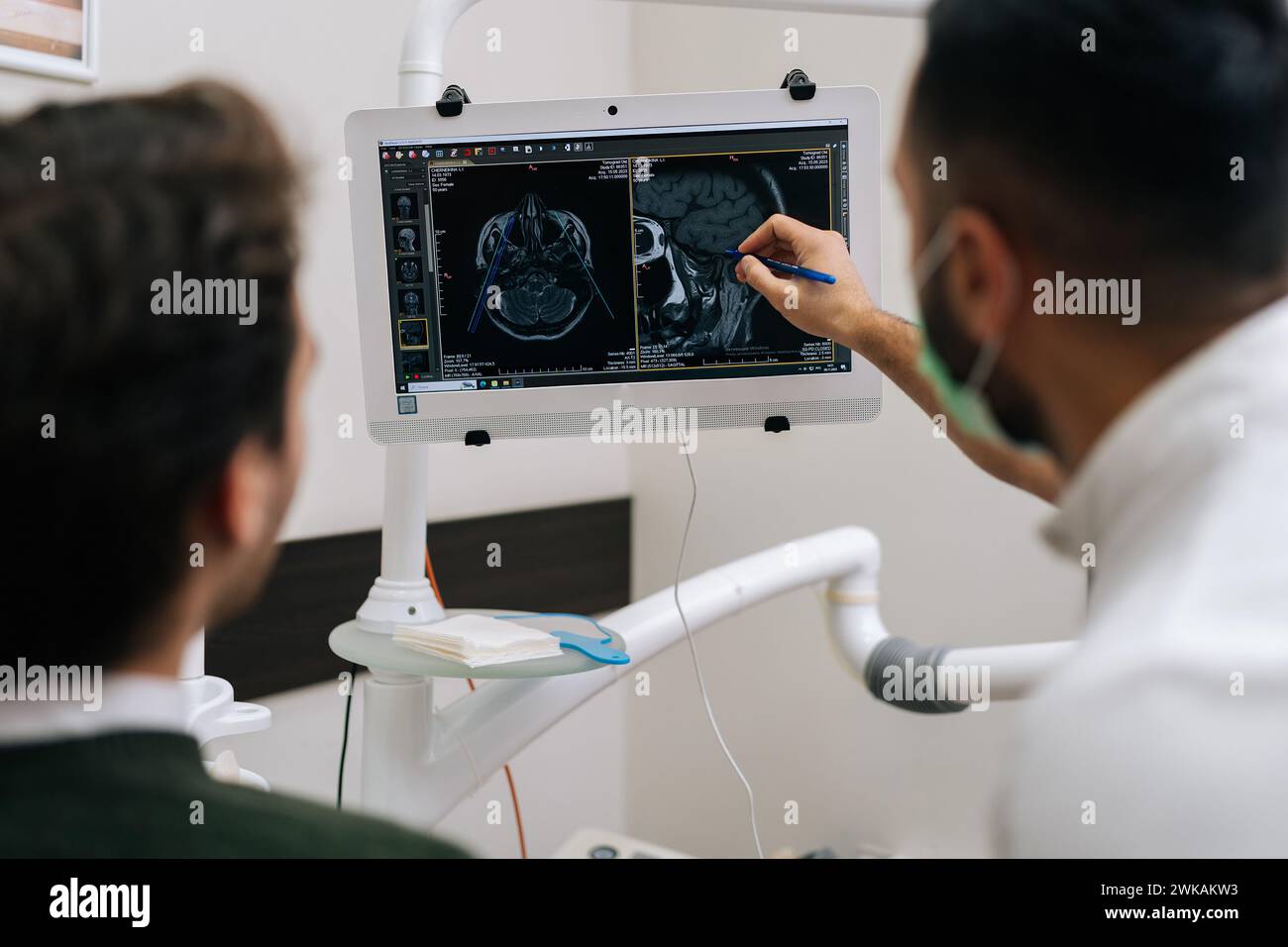 Rear view of male dentist pointing at teeth radiography on monitor to ...