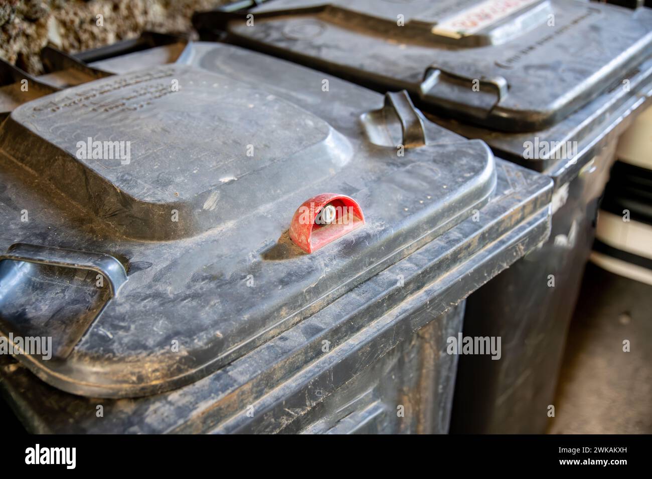 Two black garbage cans that look very used, one of which is lockable to ...